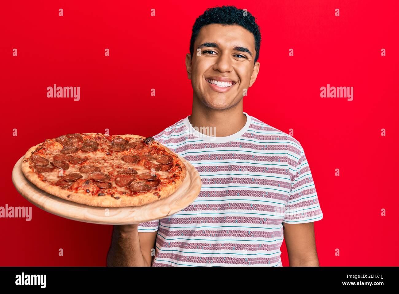 Young arab man holding italian pizza looking positive and happy ...