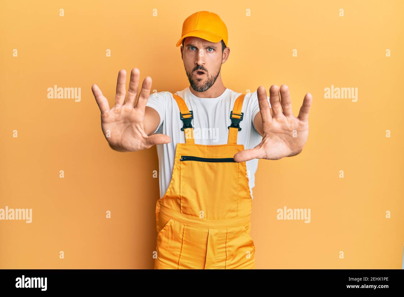 Young handsome man wearing handyman uniform over yellow background ...