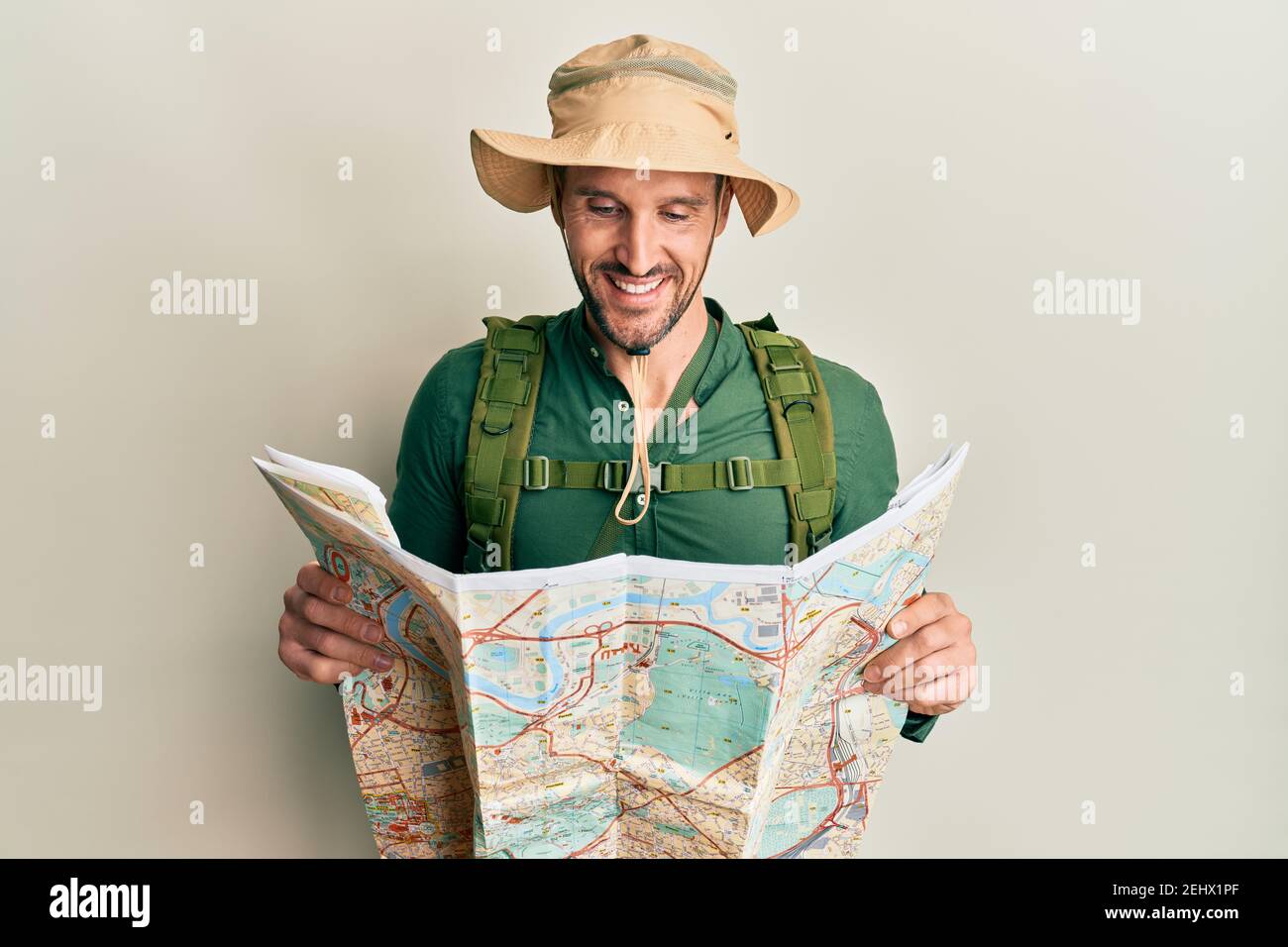 Handsome man with beard wearing explorer hat holding map smiling with a ...