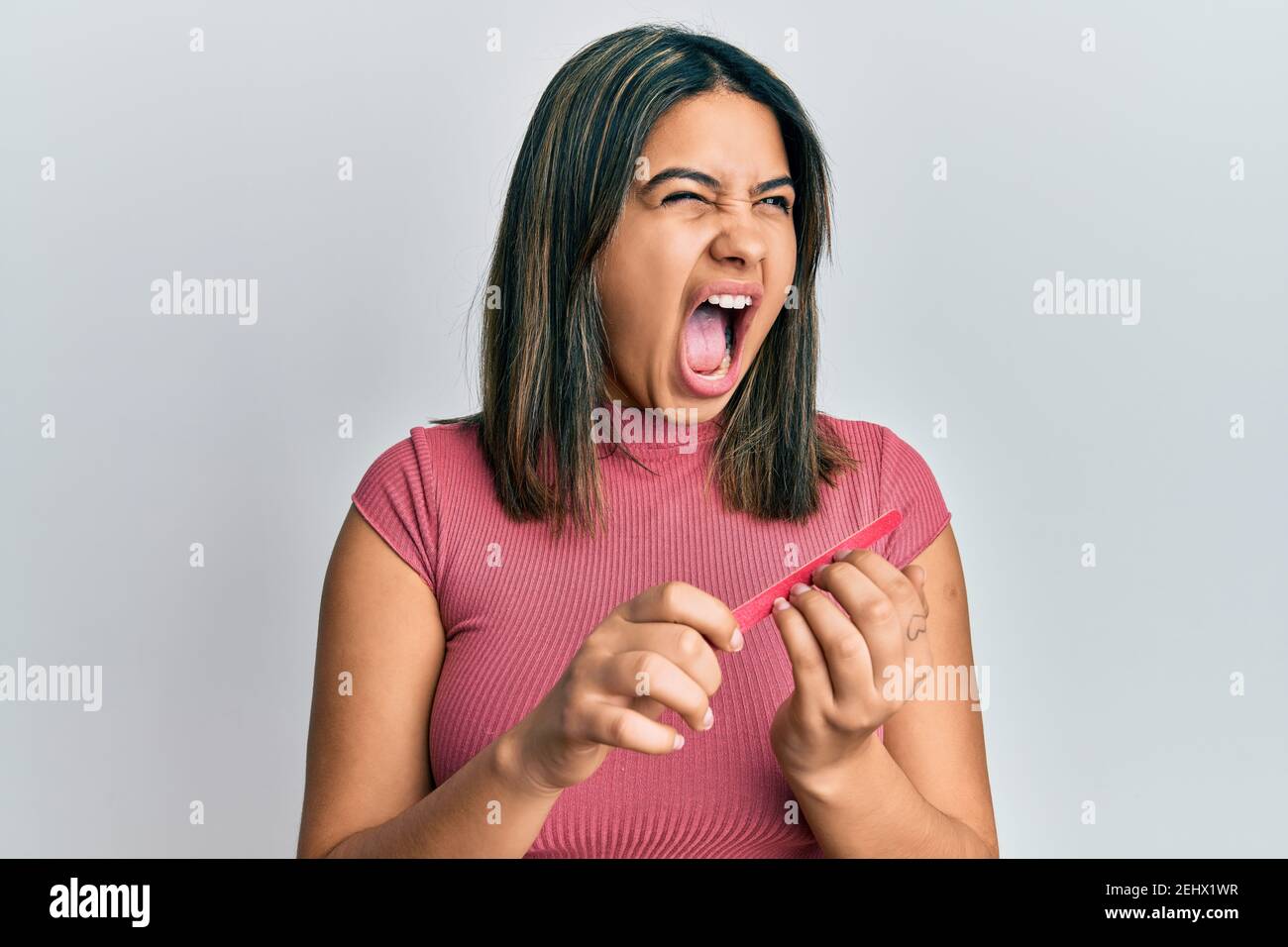 Young latin woman using file nail angry and mad screaming frustrated ...