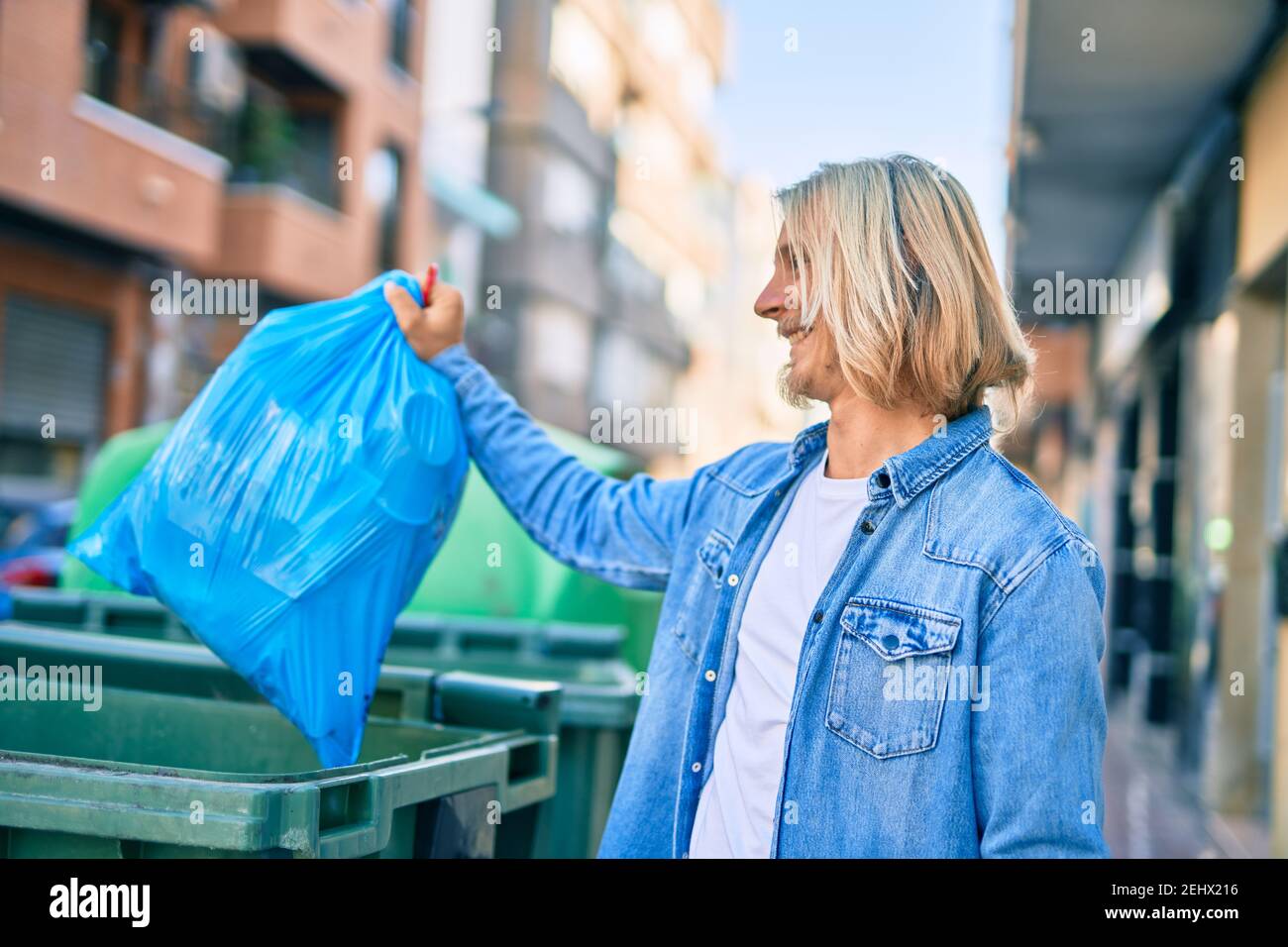 Young blond scandinavian man throwing waste bag to the container at the ...