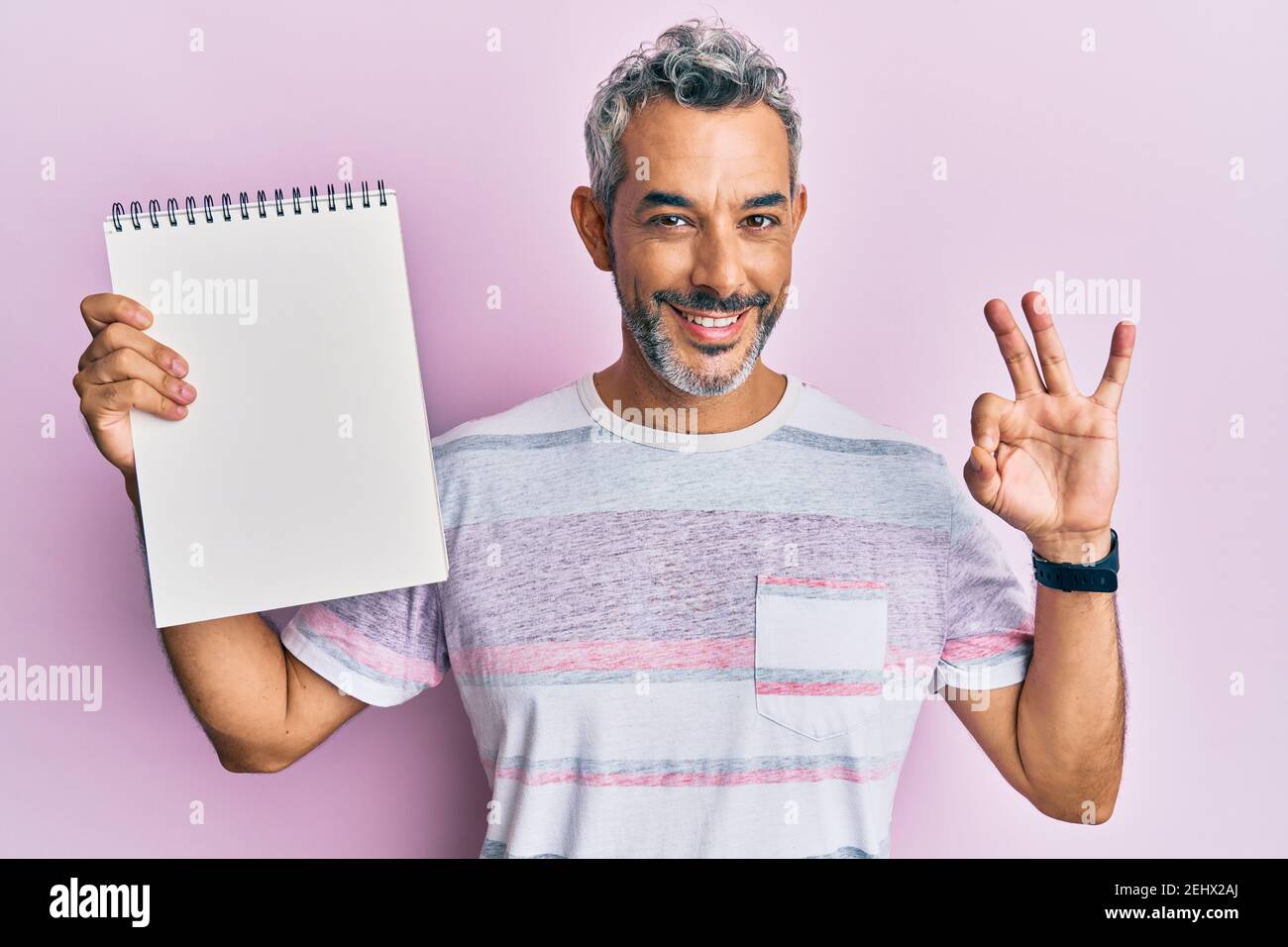 Middle age grey-haired man holding empty notebook doing ok sign with ...