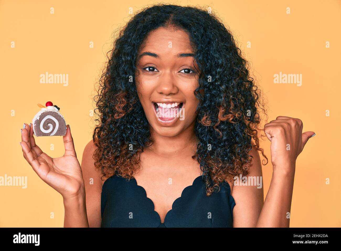 Young African American Woman Holding Cupcake Pointing Thumb Up To The