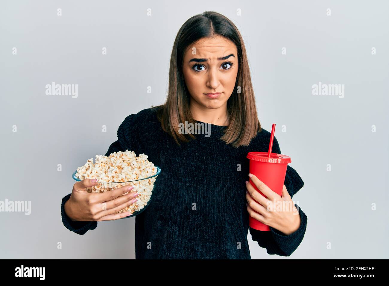 Young brunette girl eating popcorn and drinking soda clueless and ...