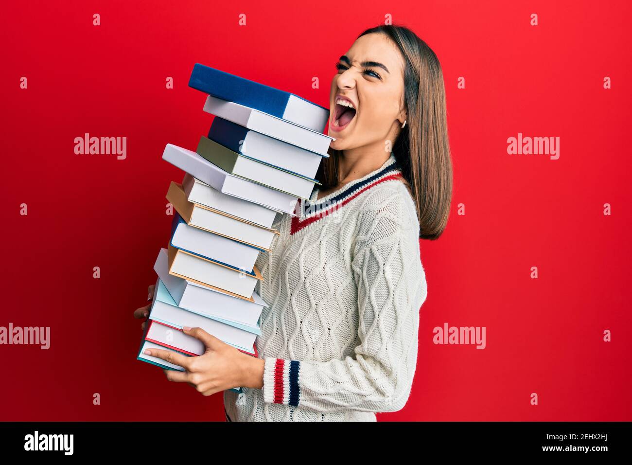 Young brunette student girl holding a pile of books angry and mad ...