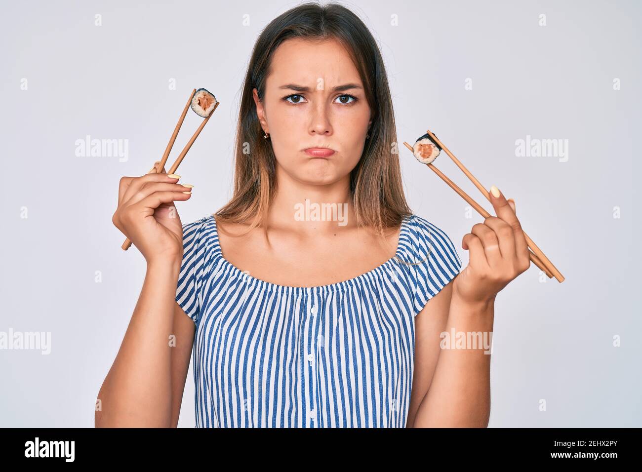 Beautiful caucasian woman eating sushi using chopsticks depressed and ...