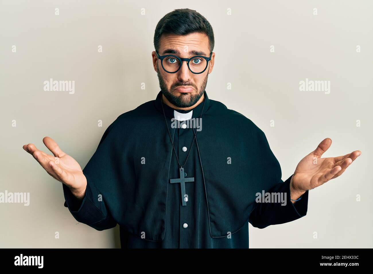 Young hispanic priest man standing over white background depressed and ...