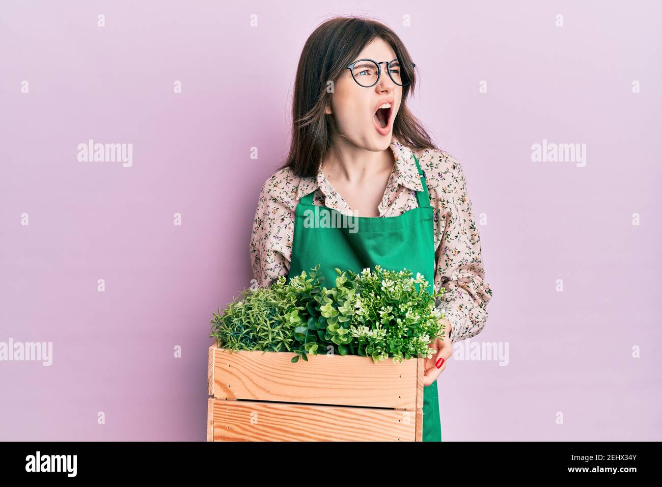 Young beautiful caucasian girl wearing gardener apron holding wooden ...