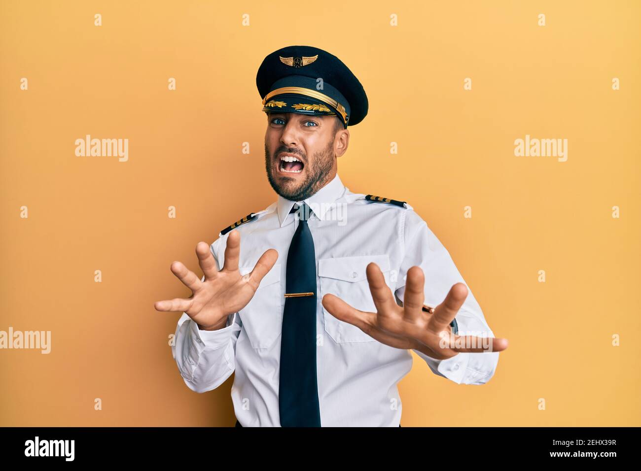 Handsome hispanic man wearing airplane pilot uniform afraid and ...