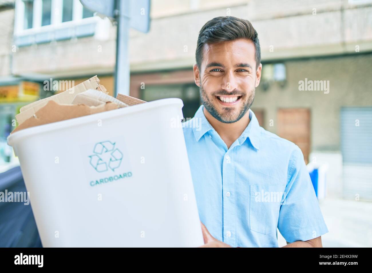 Young hispanic man smiling happy recycling. Holding full bin of ...