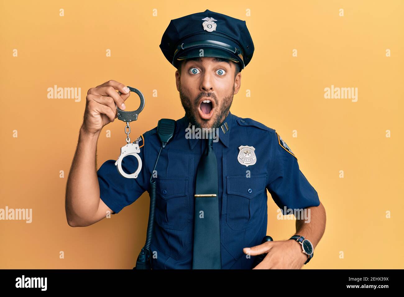 Handsome hispanic man wearing police uniform holding metal handcuffs ...