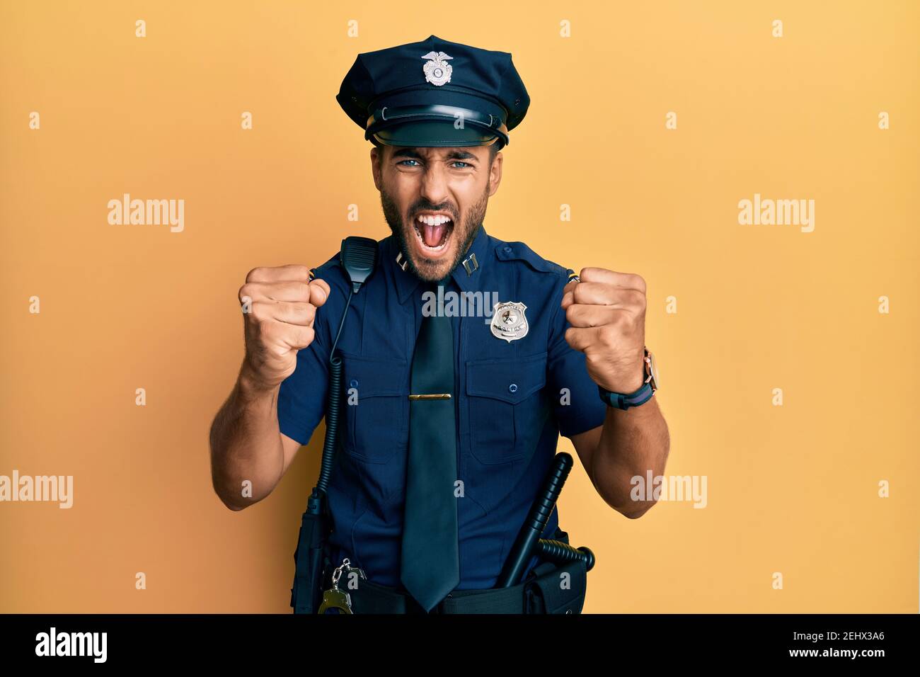 Handsome hispanic man wearing police uniform angry and mad raising ...
