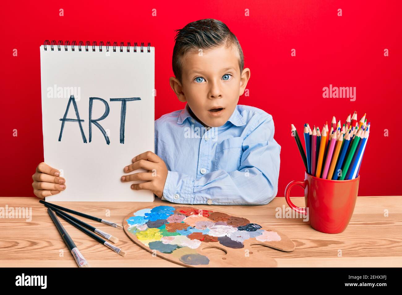 Adorable caucasian kid painter sitting at art studio holding art word ...