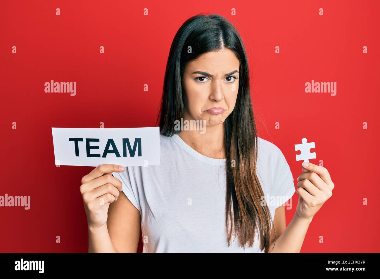 Young brunette woman holding team paper and piece of puzzle as teamwork ...