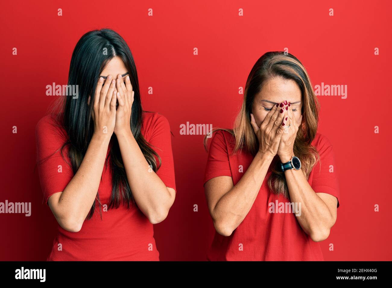 Hispanic family of mother and daughter wearing casual clothes over red ...