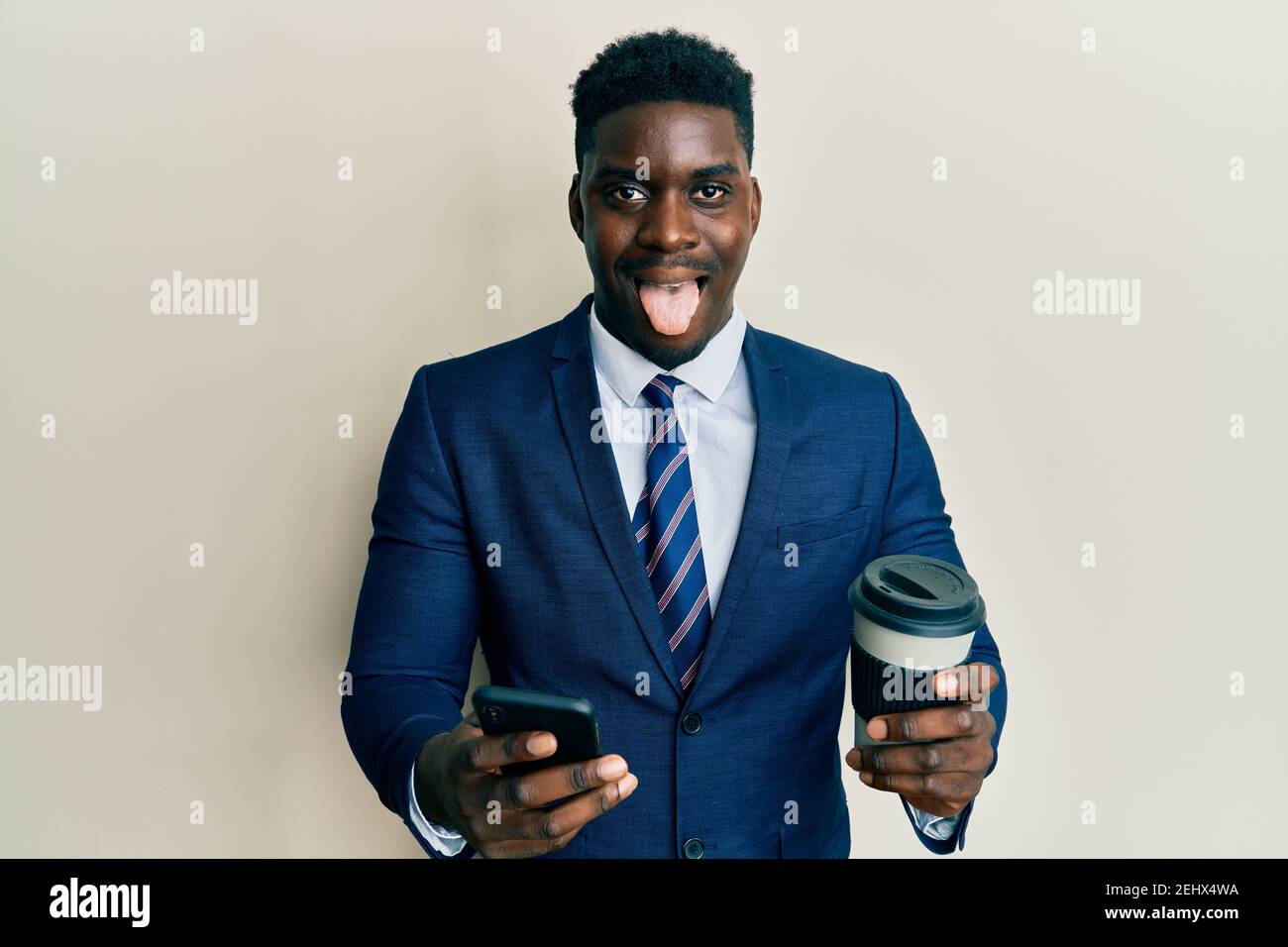 Handsome business black man using smartphone and drinking a cup of coffee sticking tongue out ...