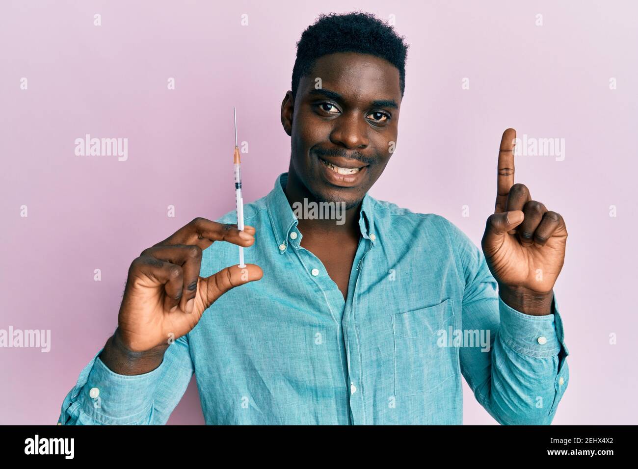 Handsome black man holding syringe surprised with an idea or question ...