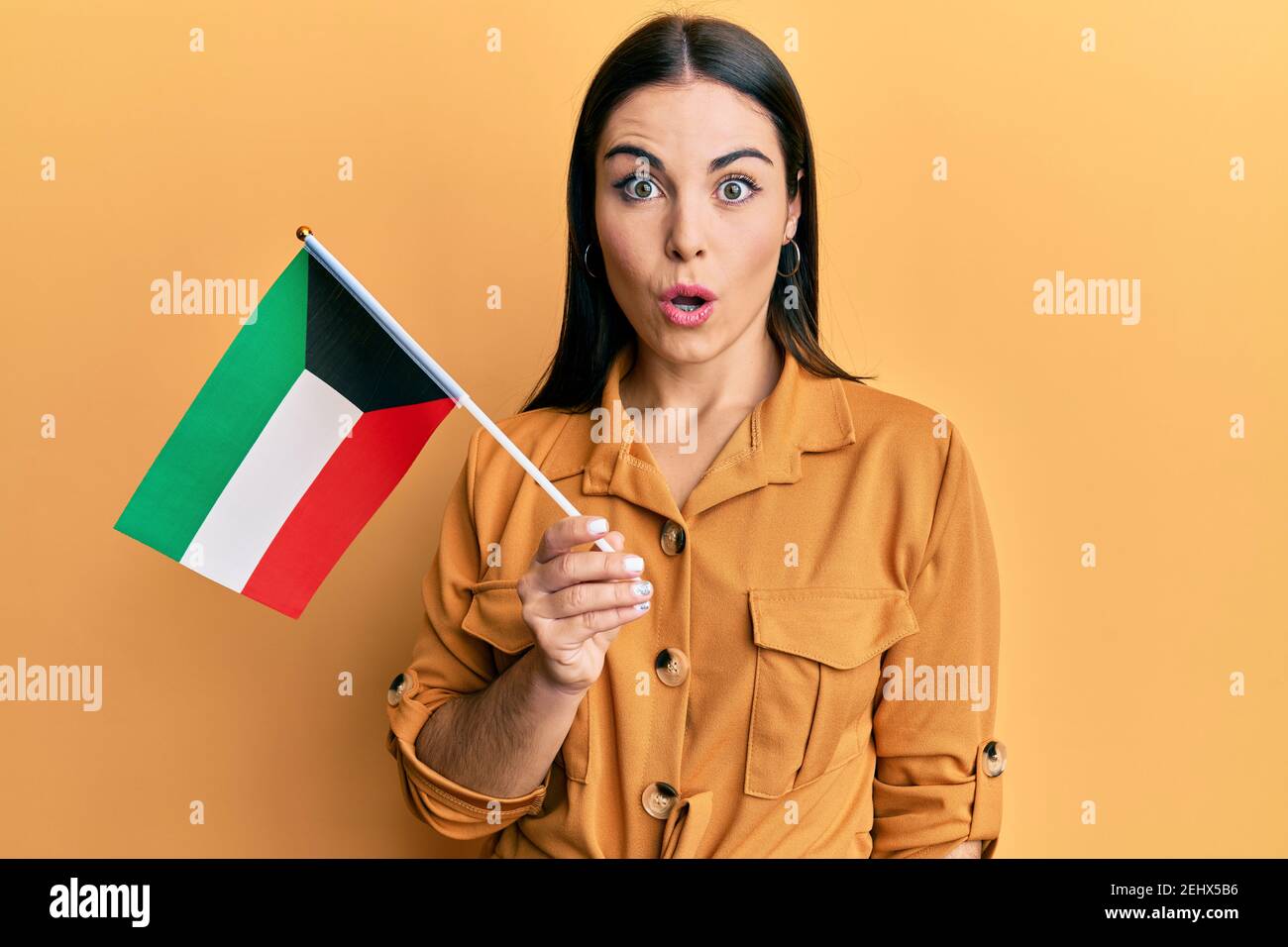 Young brunette woman holding kuwait flag scared and amazed with open ...