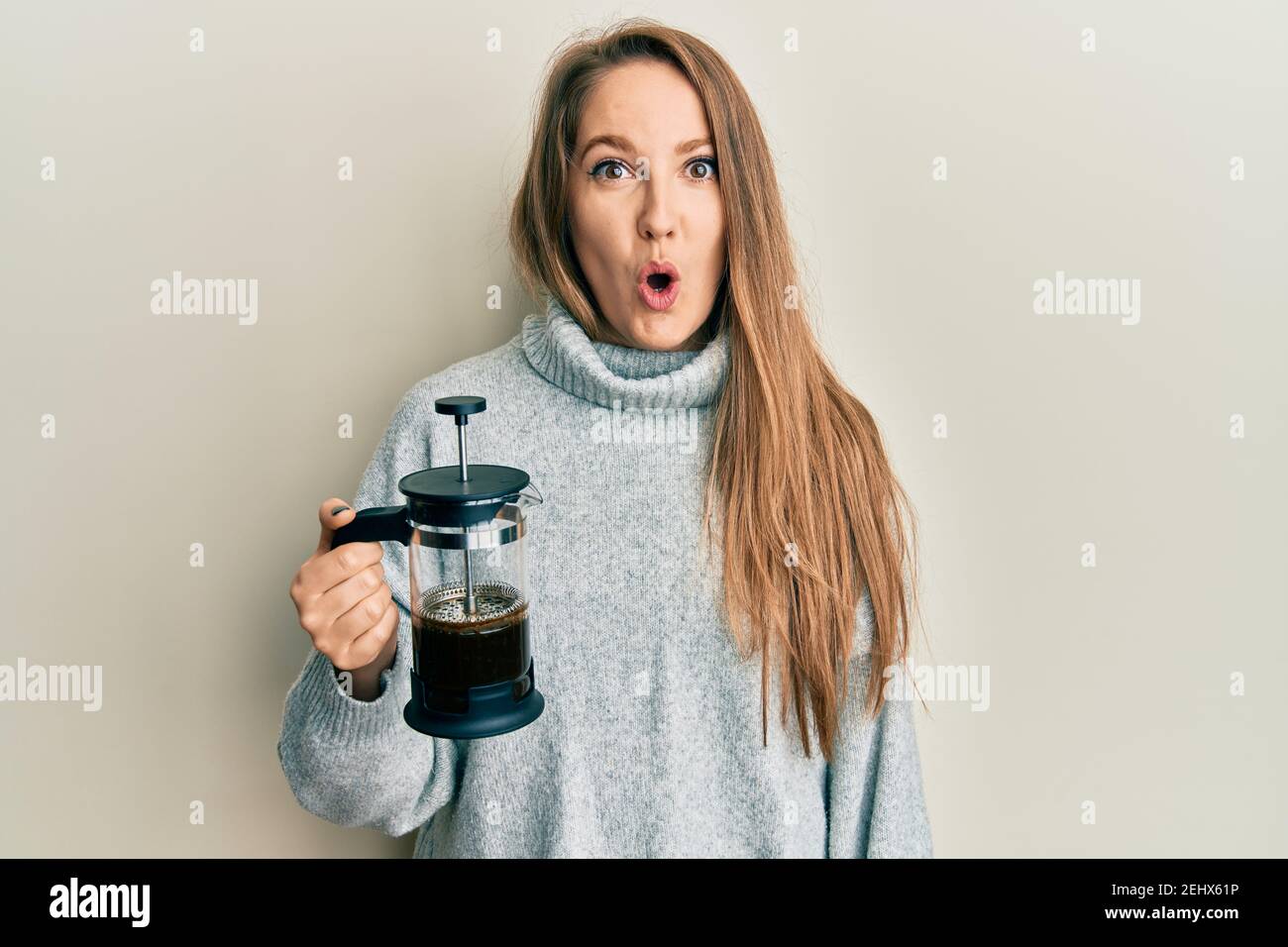 Young blonde woman drinking italian coffee scared and amazed with open ...