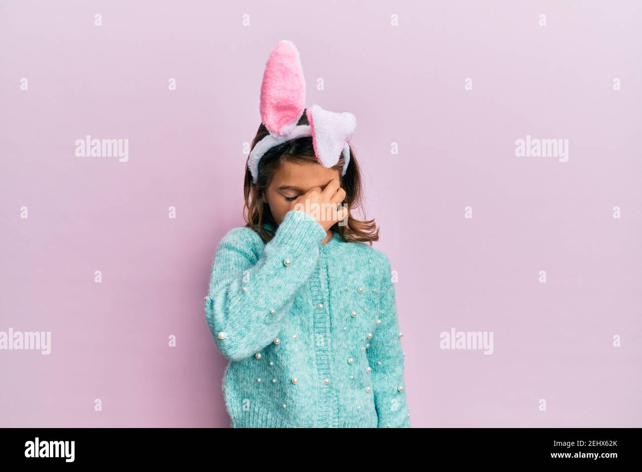 Little beautiful girl wearing cute easter bunny ears tired rubbing nose ...