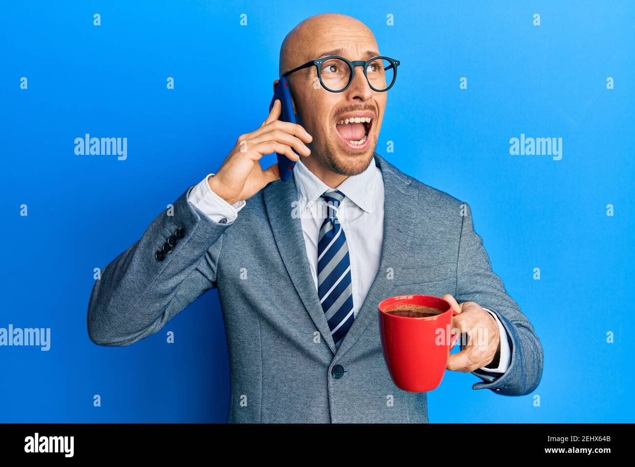 Bald man with beard using smartphone and drinking a cup of coffee angry ...