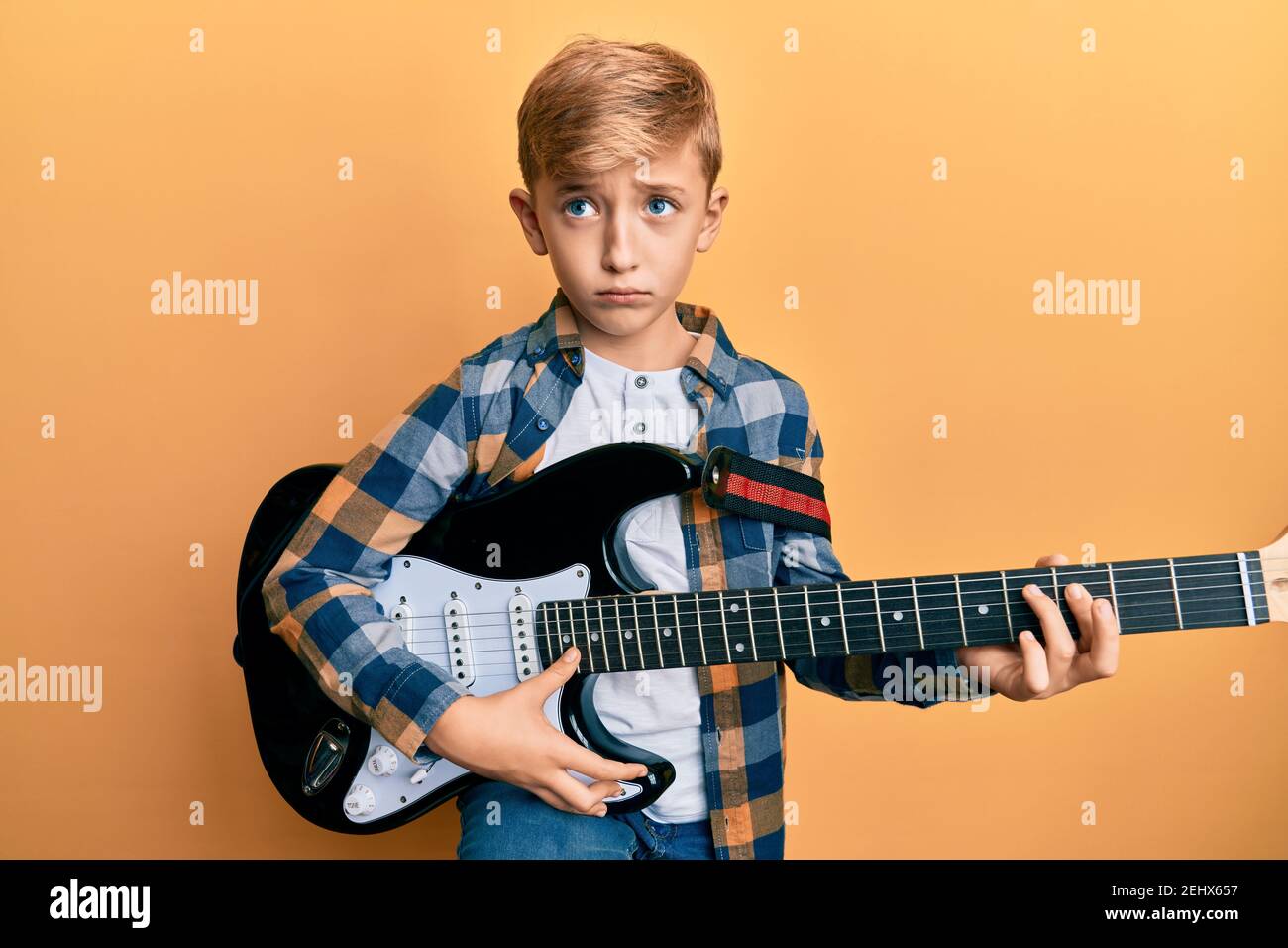 Little caucasian boy kid playing electric guitar skeptic and nervous ...