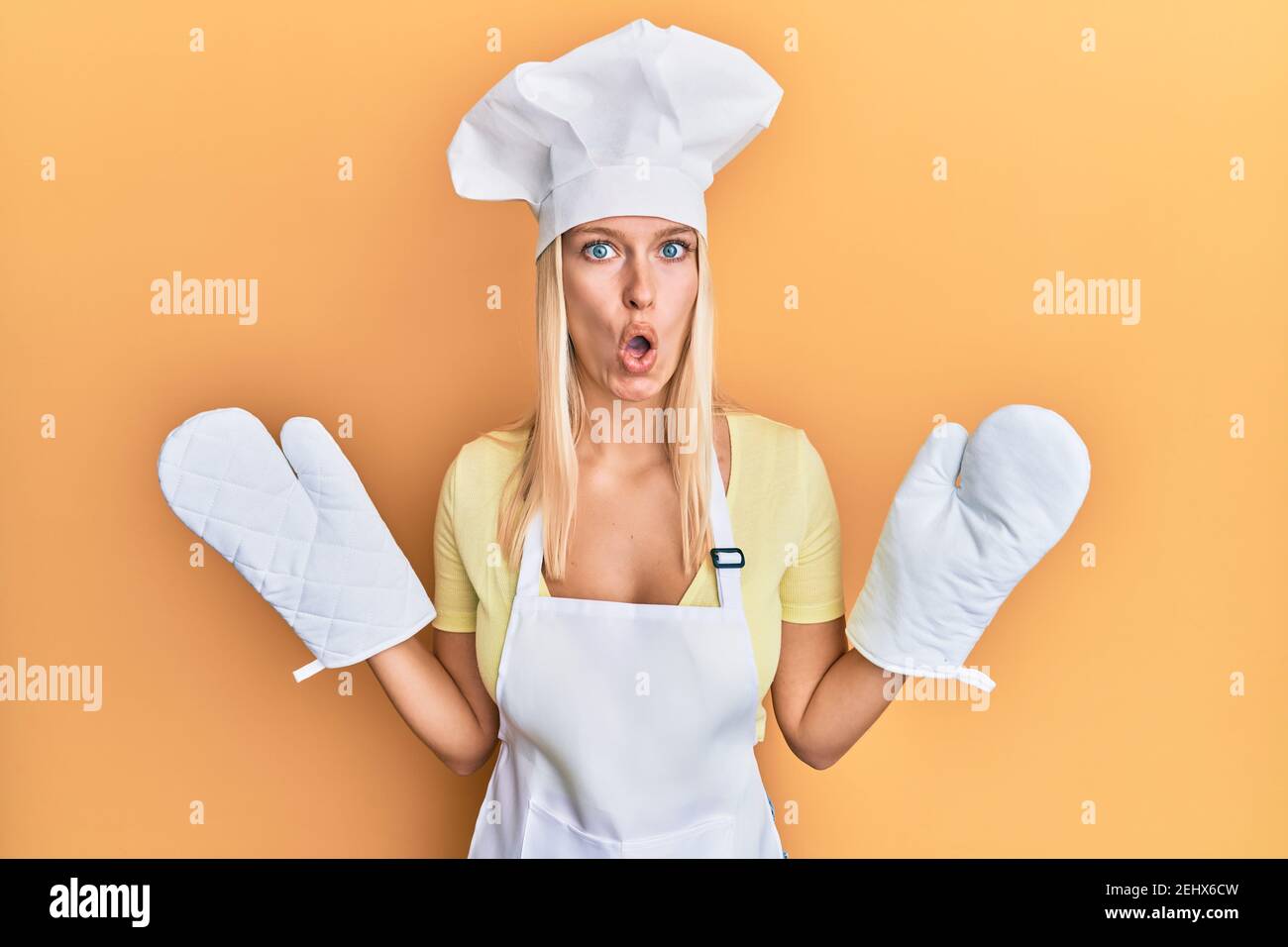 Young blonde girl wearing baker uniform and cook hat afraid and shocked ...