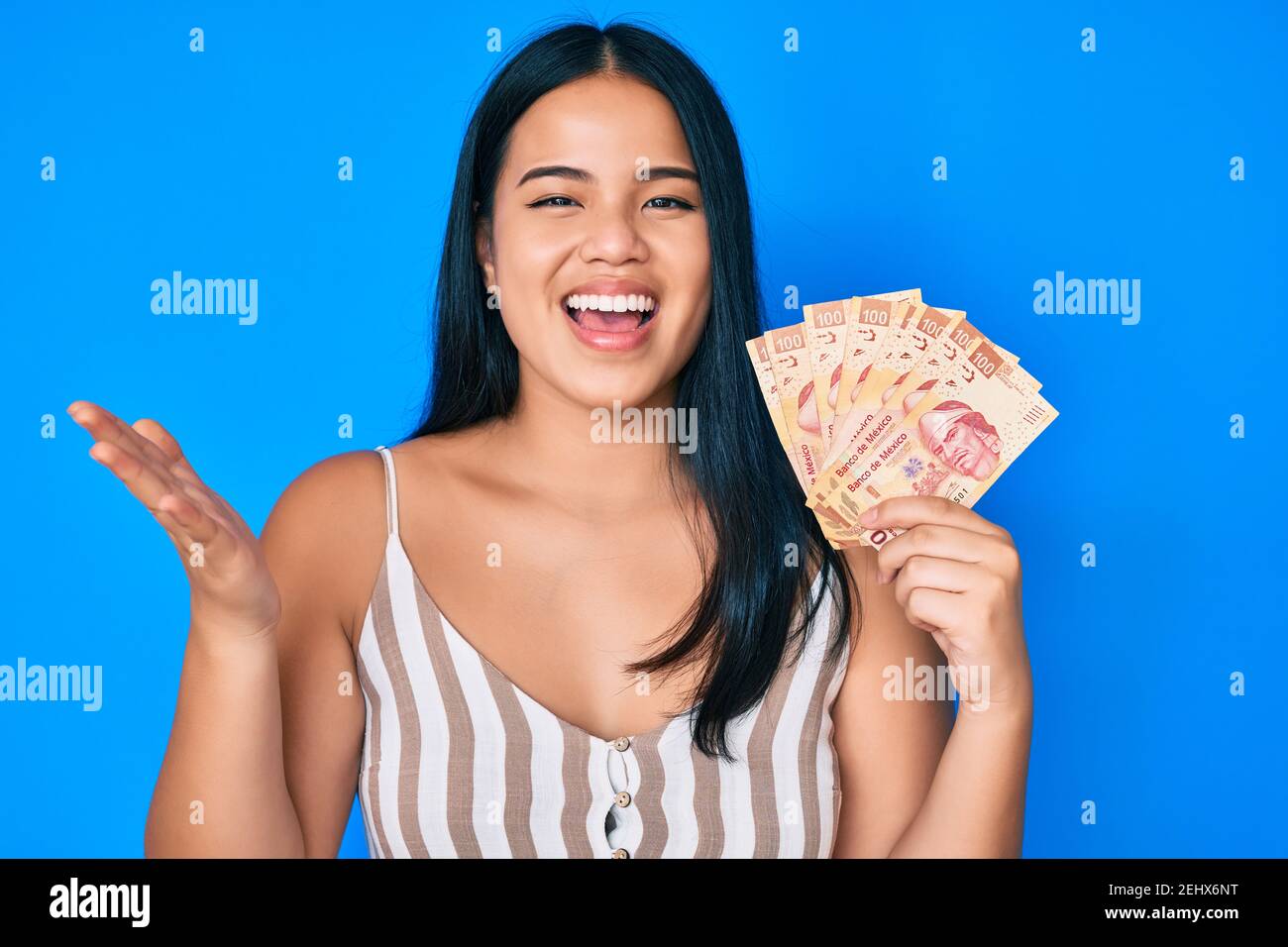 Young beautiful asian girl holding mexican pesos celebrating ...