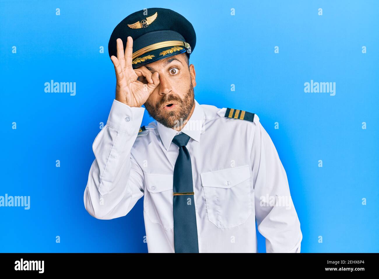 Handsome man with beard wearing airplane pilot uniform doing ok gesture ...