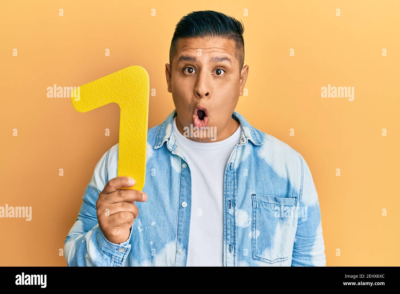 Young latin man holding number one scared and amazed with open mouth ...