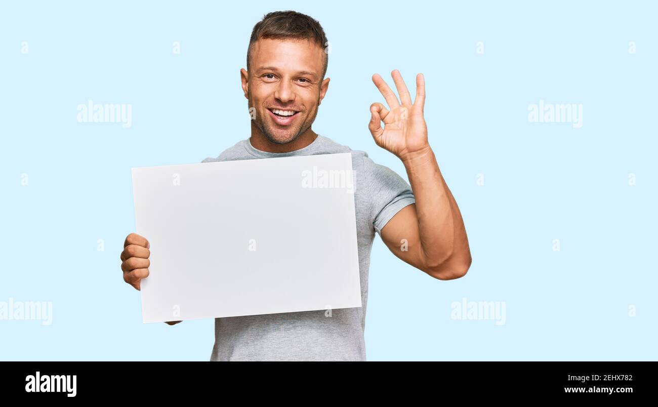 Handsome muscle man holding blank empty banner doing ok sign with ...