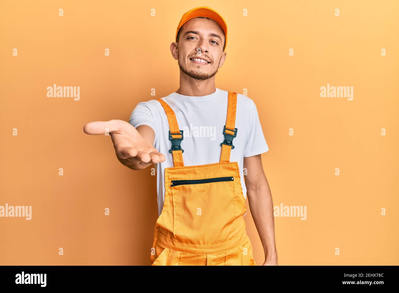 Hispanic young man wearing handyman uniform smiling friendly offering ...