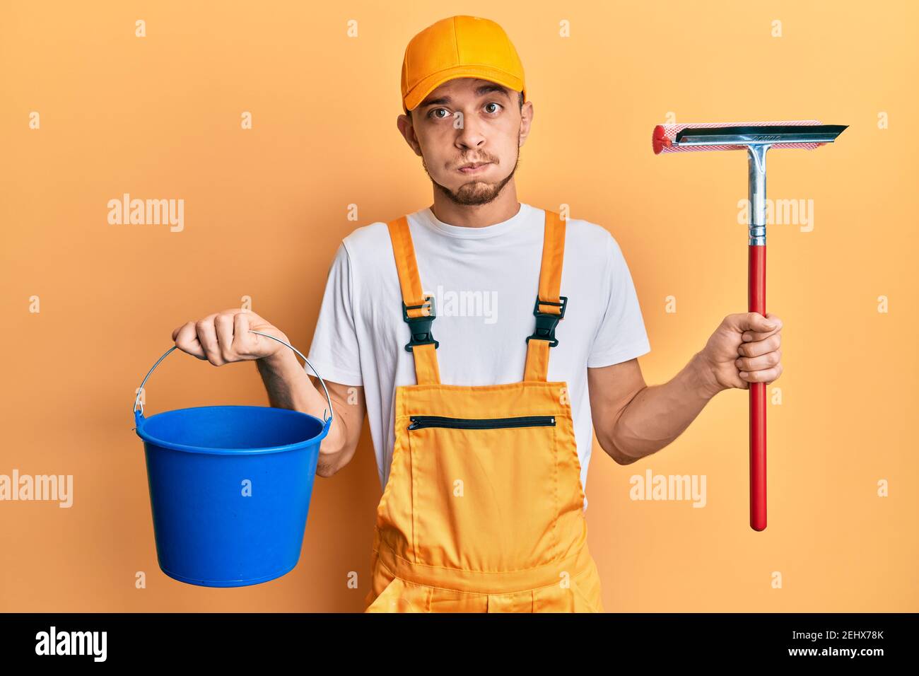 Hispanic young man wearing glass cleaner uniform and squeegee puffing ...