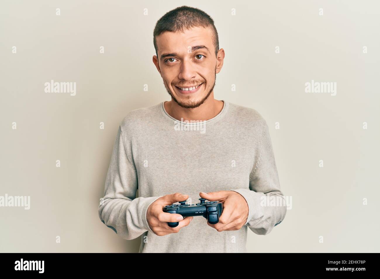 Hispanic young man playing video game holding controller smiling with a ...
