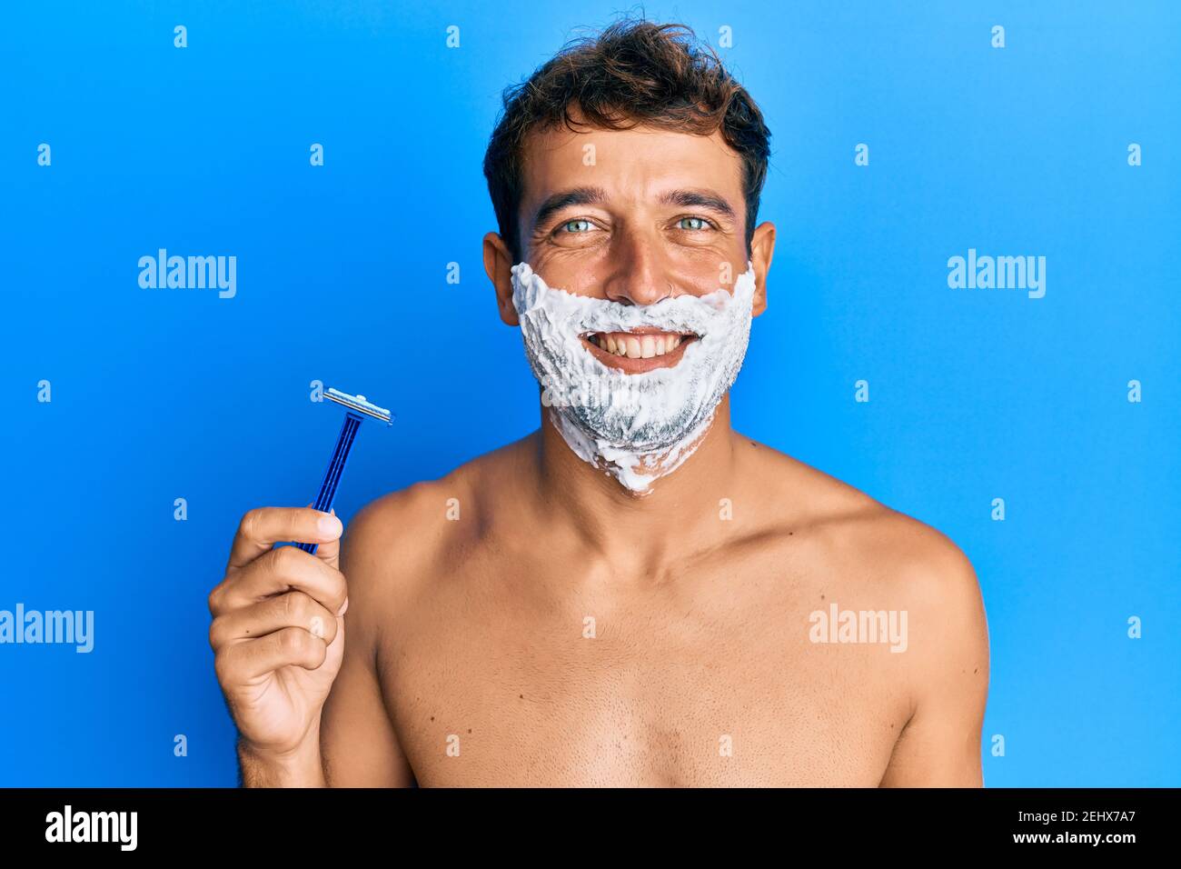 Handsome man saving beard with shave foam over face holding razor ...