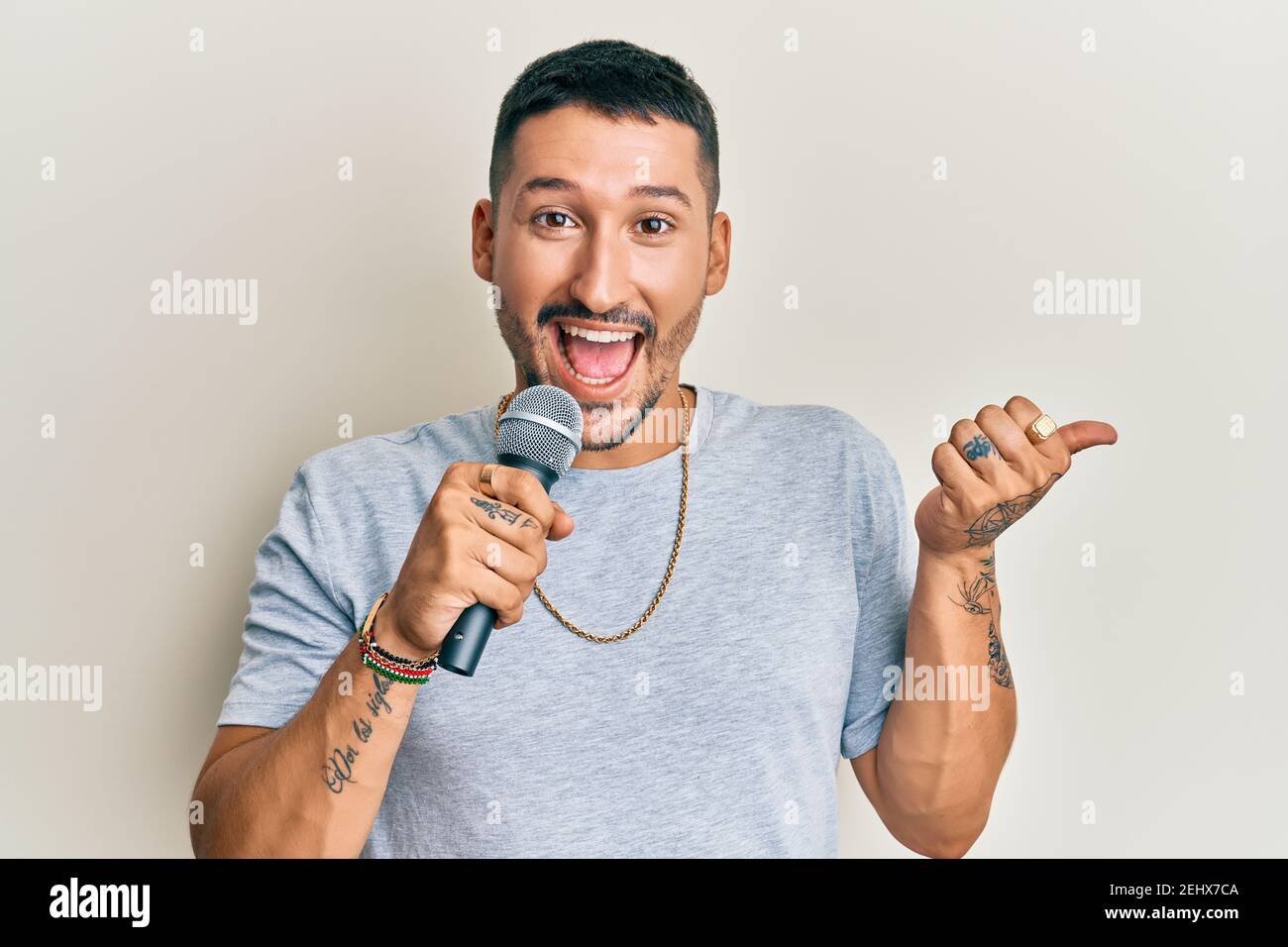 Handsome man with tattoos singing song using microphone pointing thumb ...