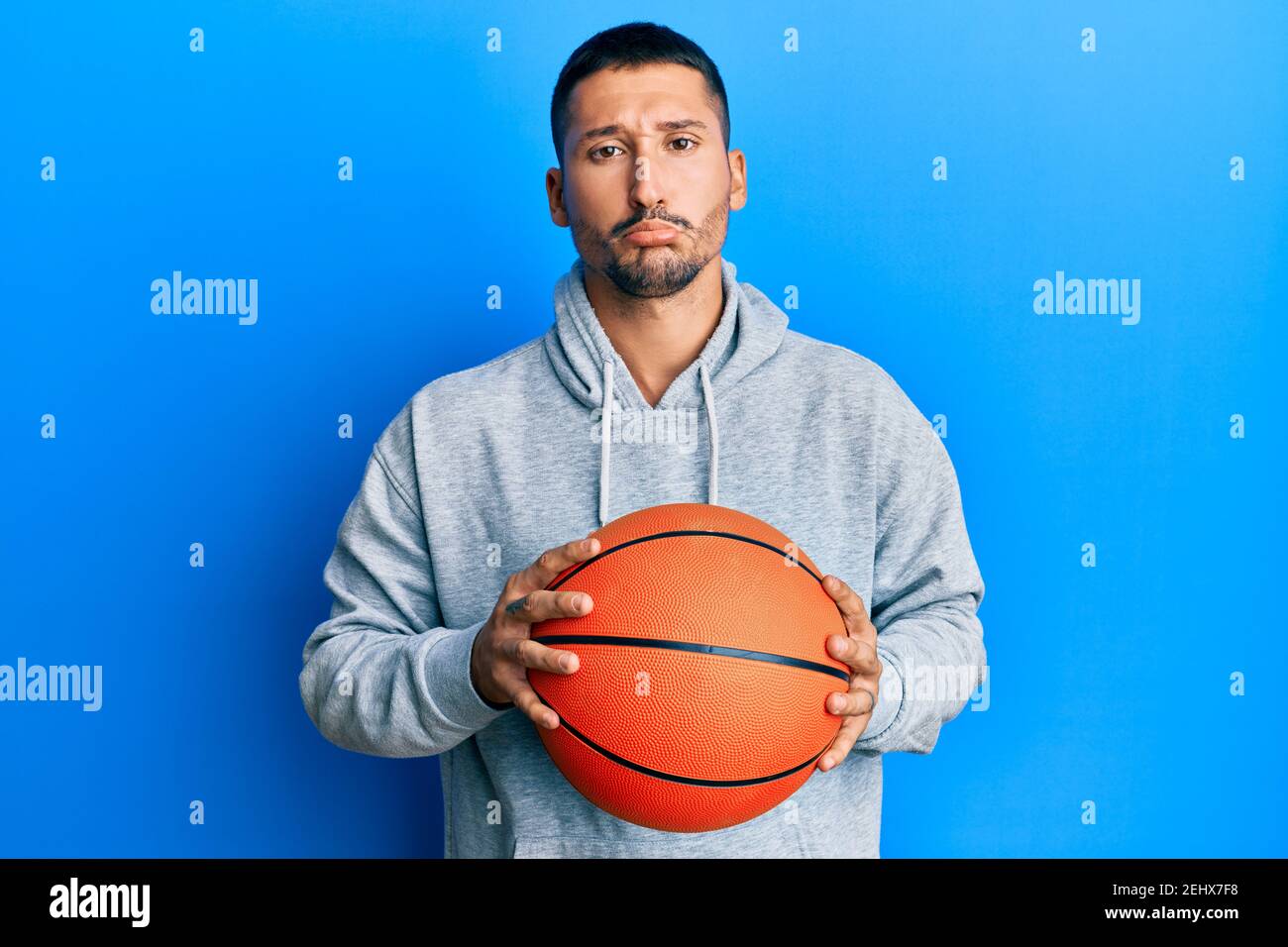 Handsome man with tattoos holding basketball ball depressed and worry ...