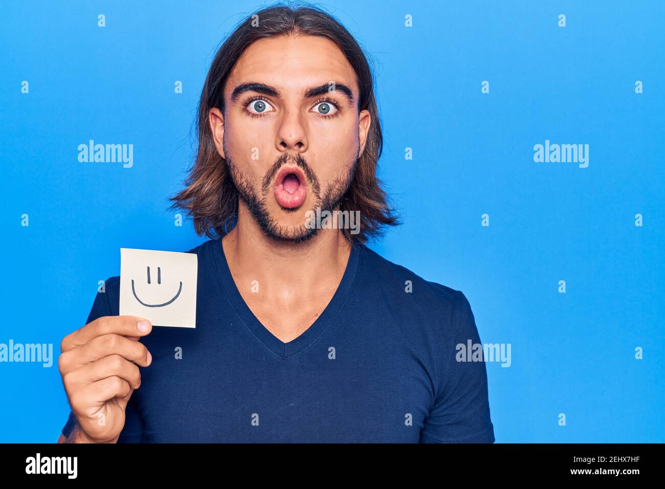 Young handsome man holding smile emoji reminder scared and amazed with ...