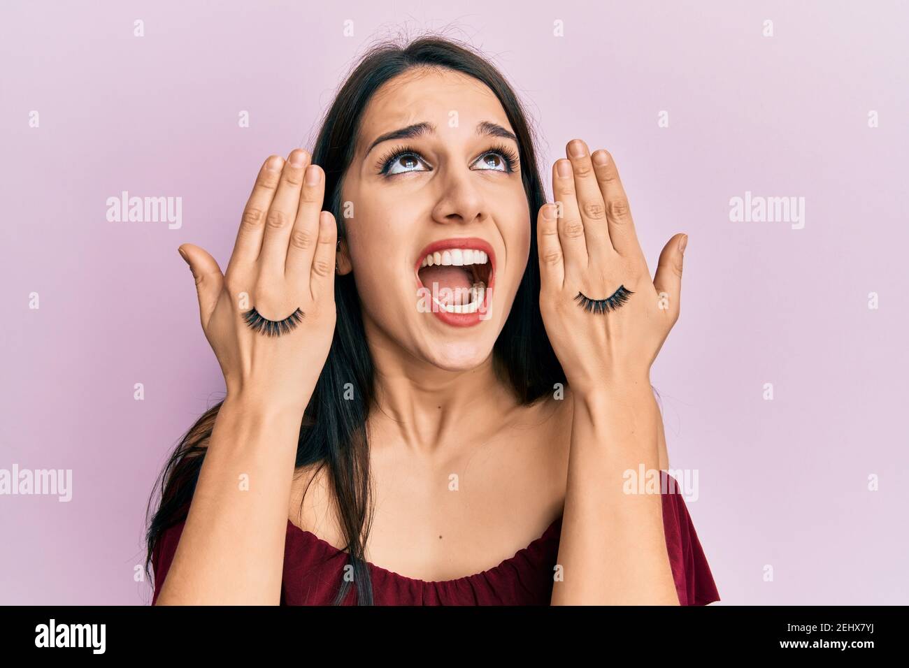 Young hispanic woman covering eyes with hands and fake lashes angry and ...