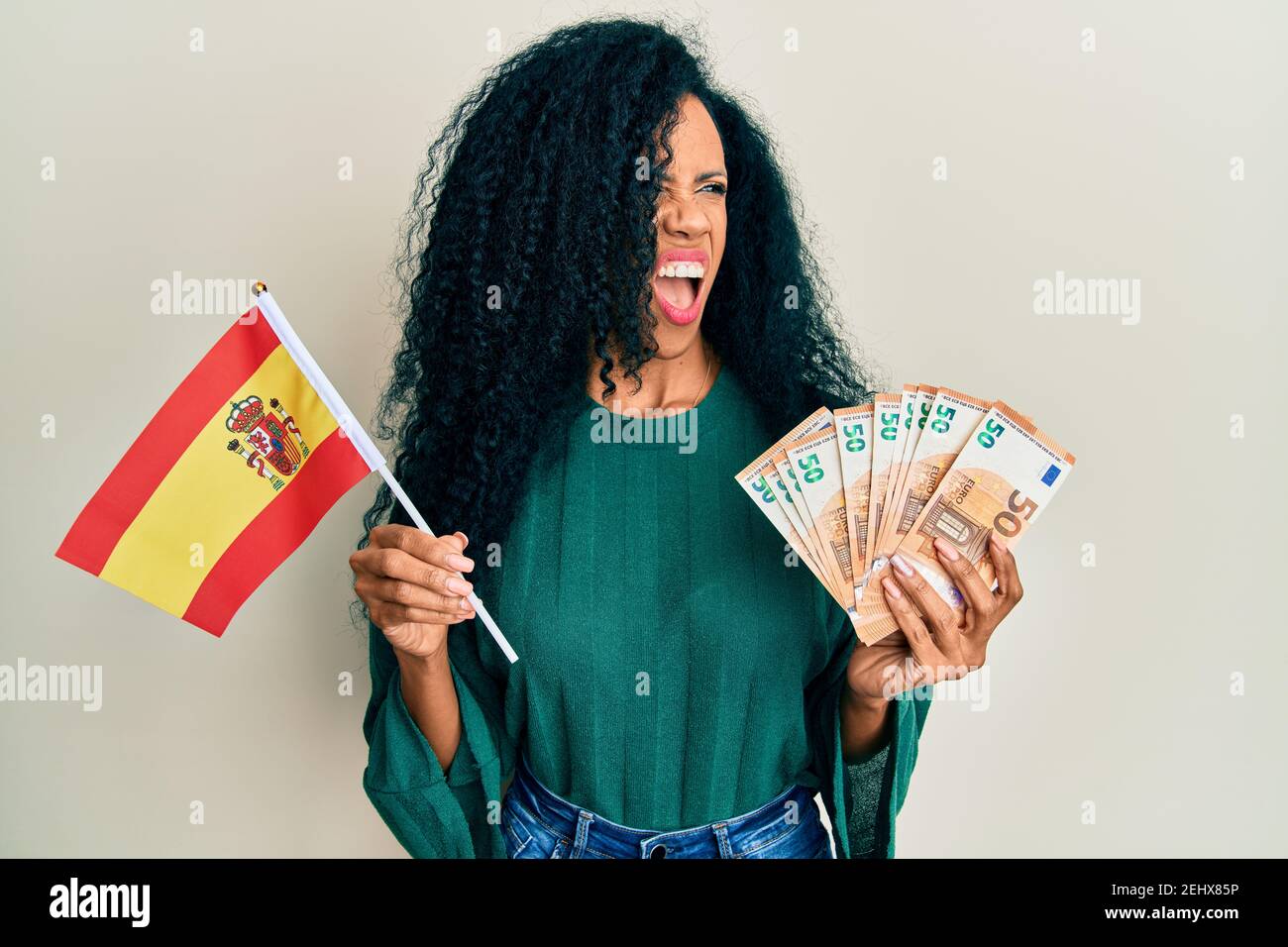Middle age african american woman holding spain flag and euros ...