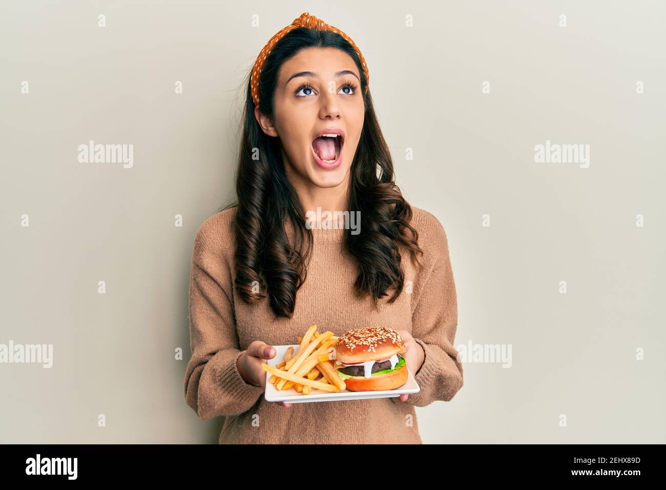 Young hispanic woman eating a tasty classic burger angry and mad ...