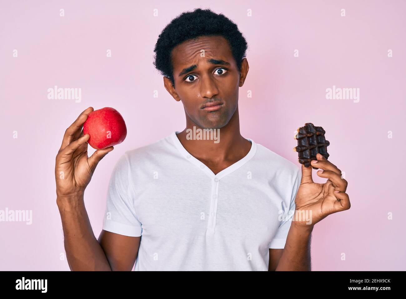 Handsome african man holding red apple and chocolate waffle depressed ...