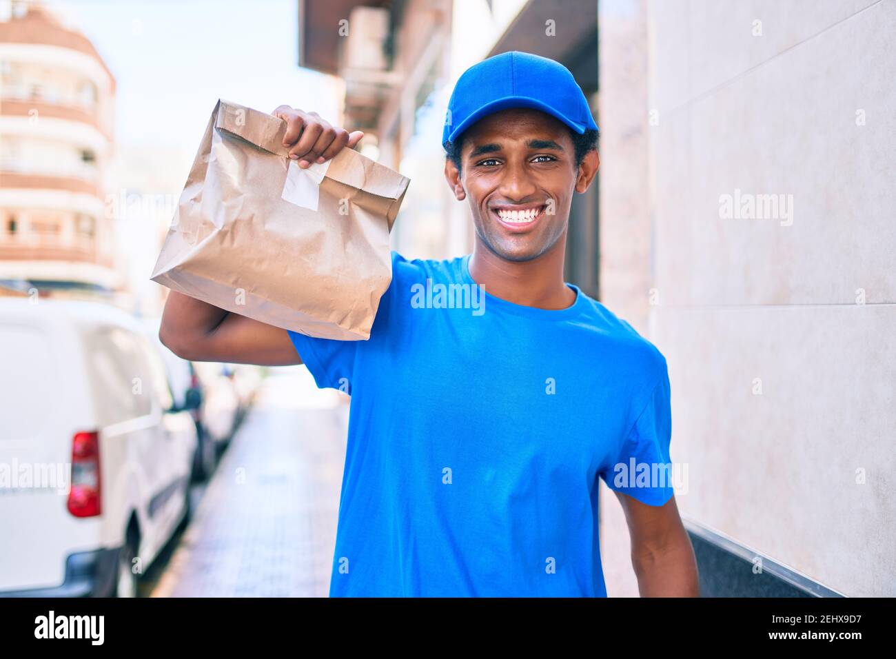 African delivery man wearing courier uniform outdoors holding take away ...