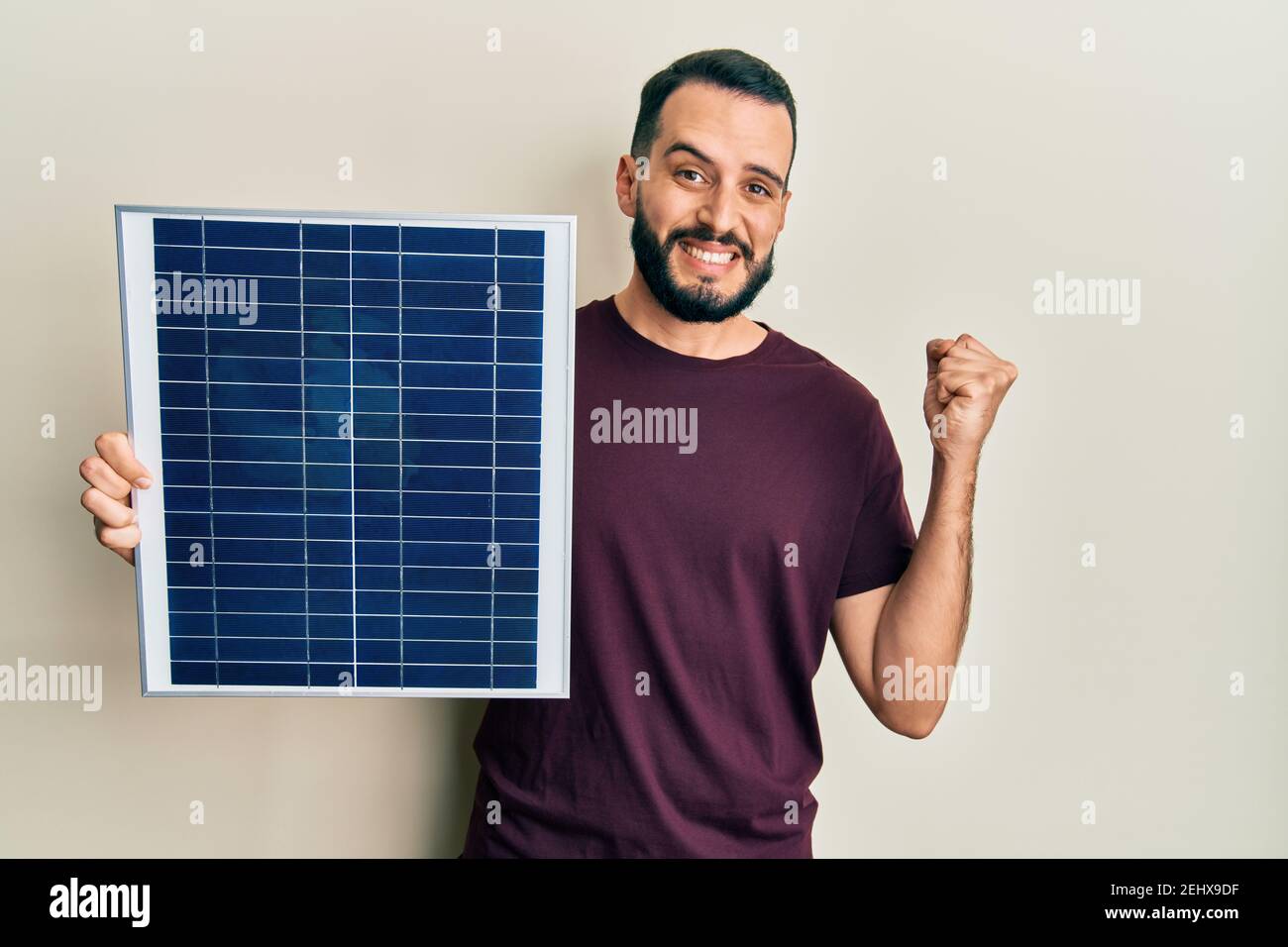 Young man with beard holding photovoltaic solar panel screaming proud ...