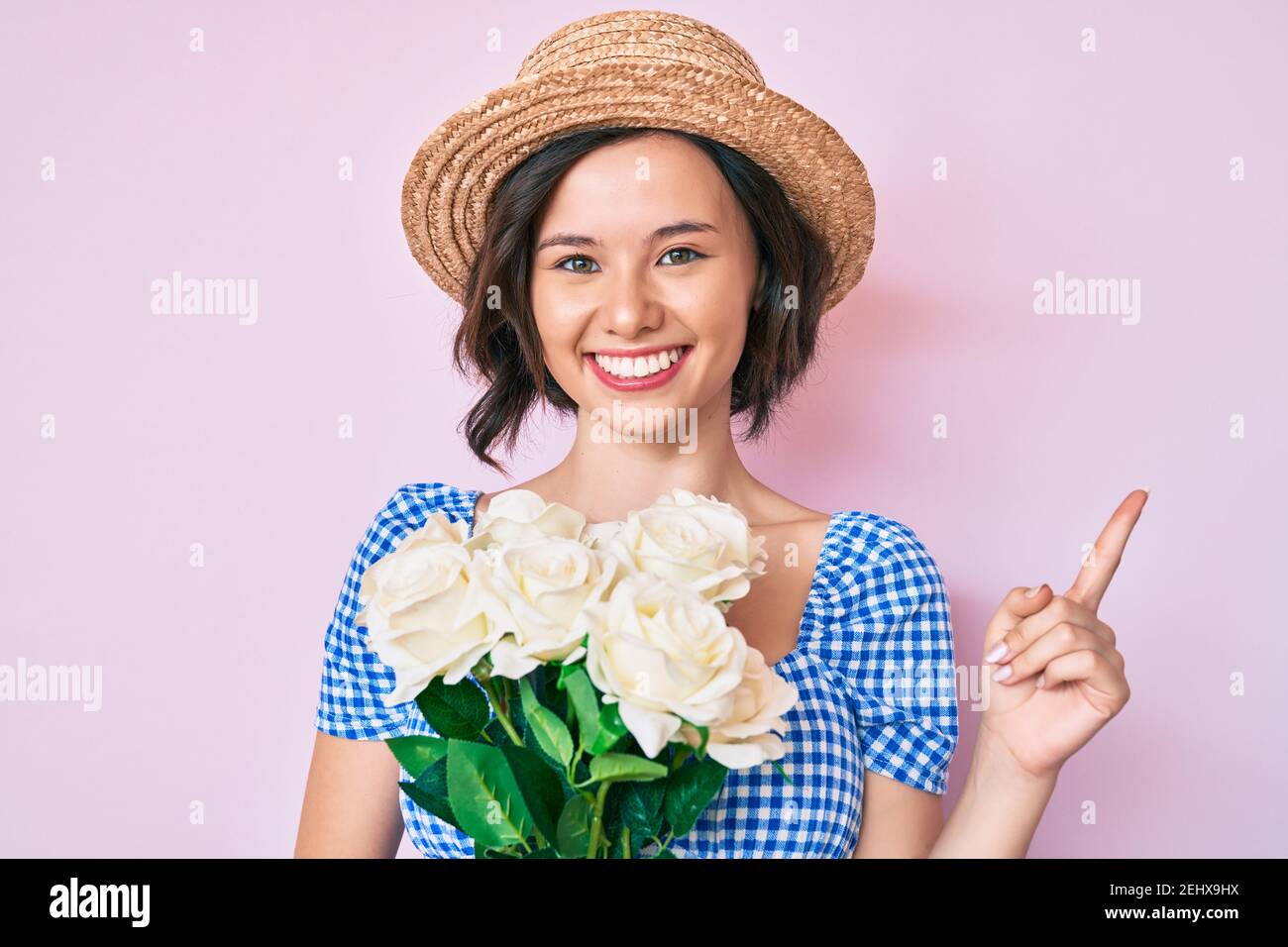Young beautiful girl wearing summer hat holding flowers smiling happy ...