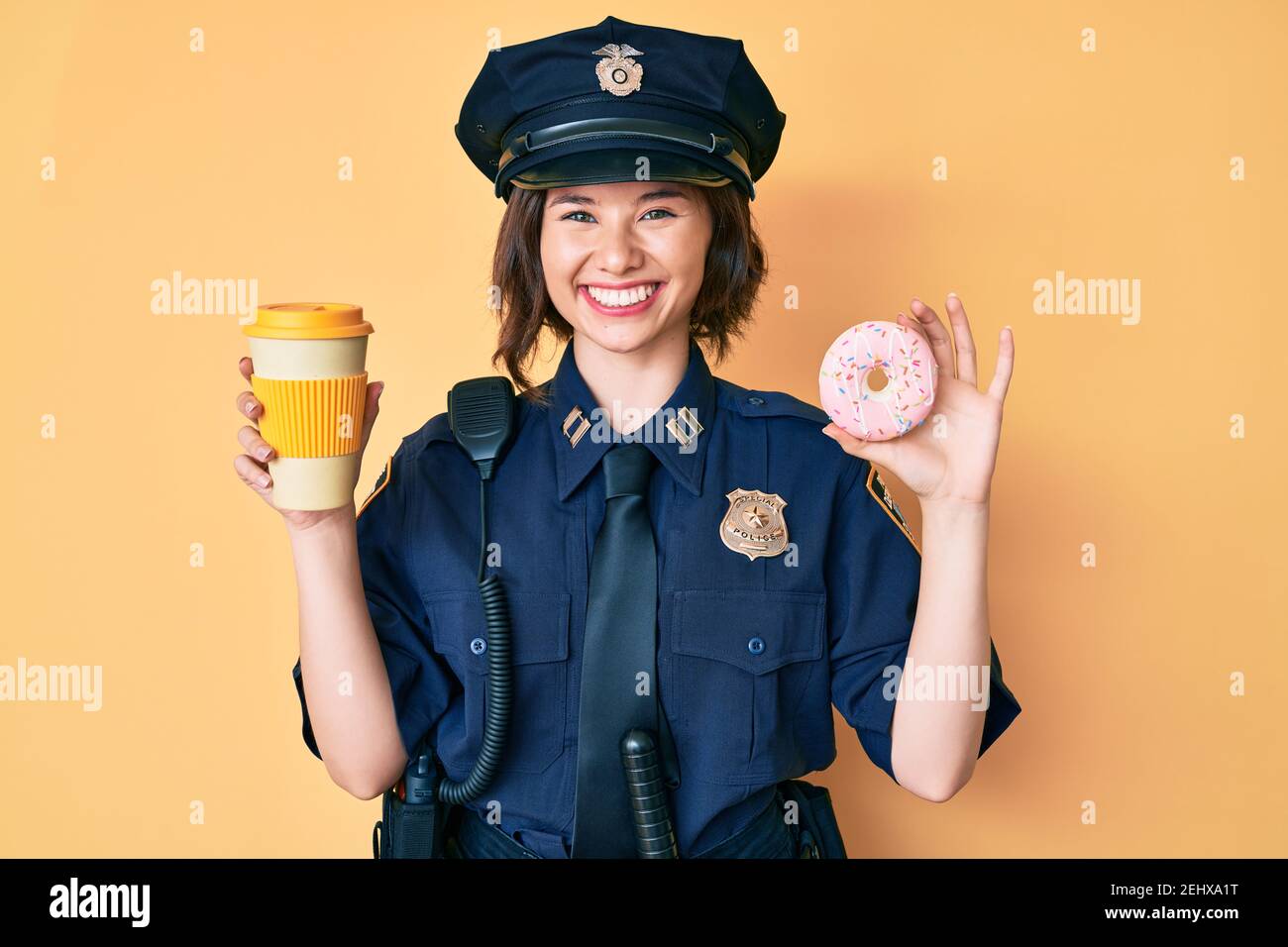 Young beautiful woman wearing police uniform holding donut and take ...