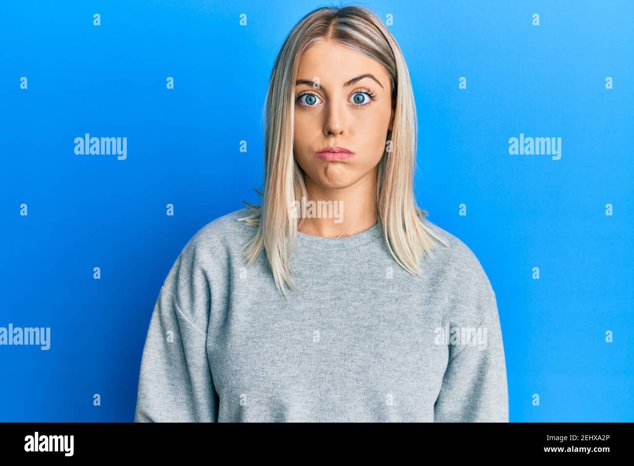 Beautiful blonde woman wearing casual clothes puffing cheeks with funny ...