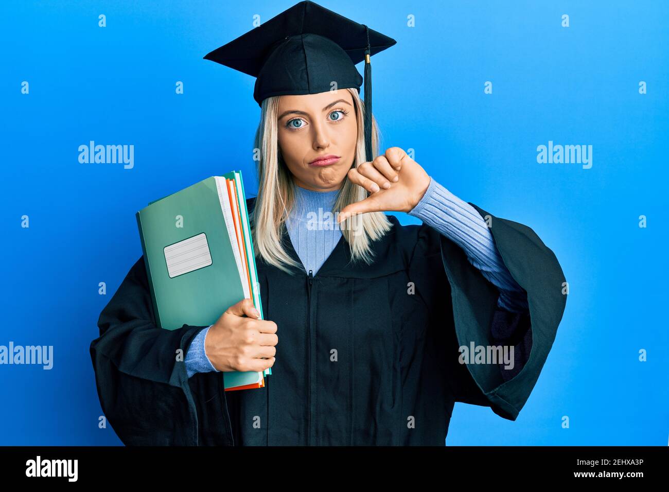 Beautiful blonde woman wearing graduation cap and ceremony robe holding ...