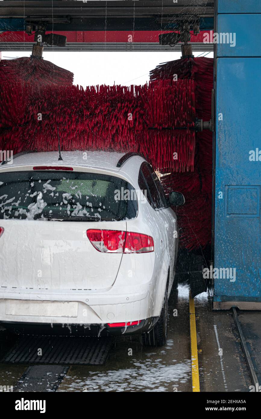 white car washing in automatic car wash with red rollers and lots of ...