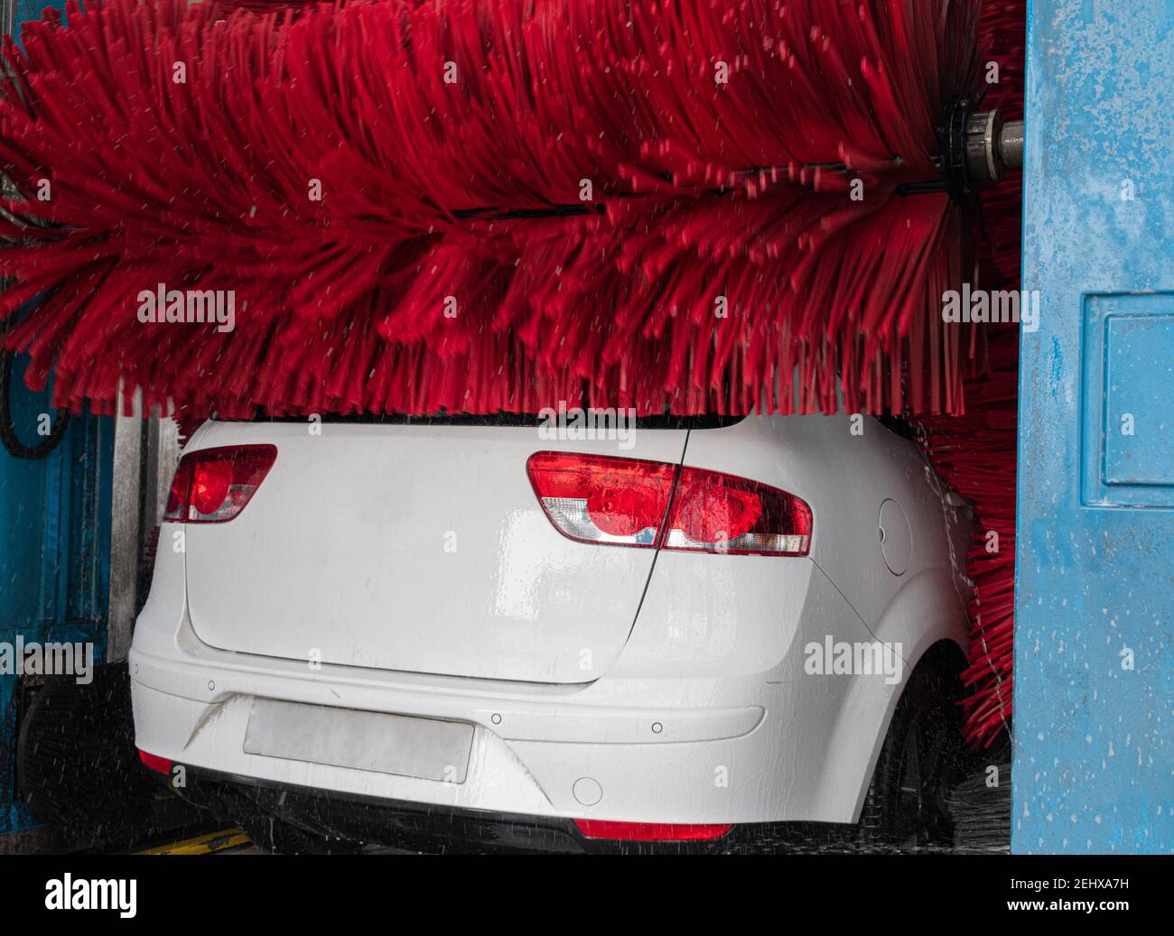 white car washing in automatic car wash with red rollers and lots of ...